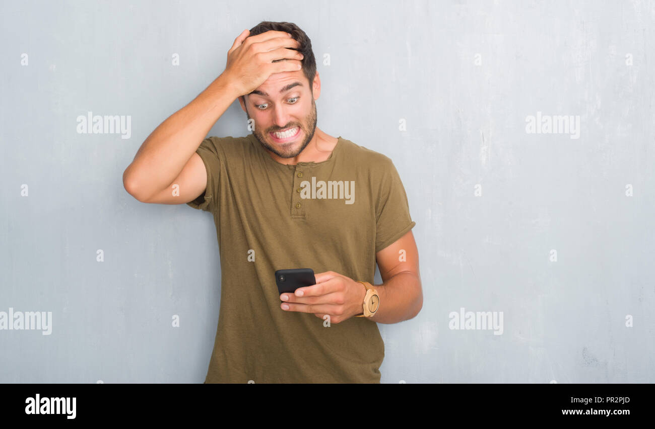 Handsome young man over grey grunge wall texting a message using ...