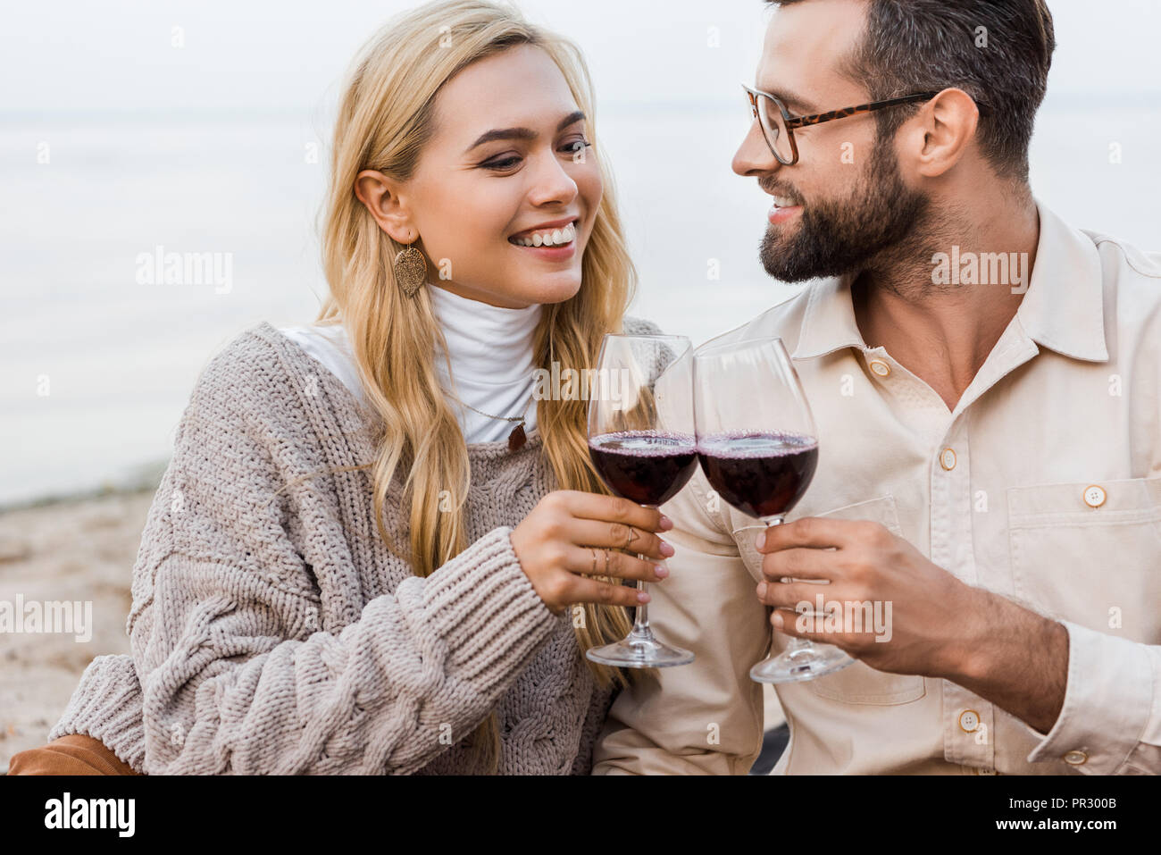 portrait of happy boyfriend and girlfriend in autumn outfit clinking with glasses on beach Stock ...