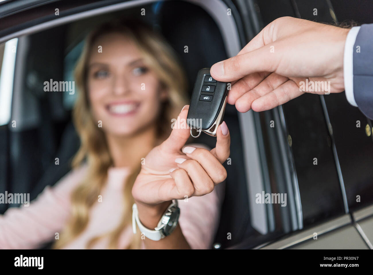 partial view of dealership salon seller giving car key to smiling woman ... partial view of dealership salon seller giving car key to smiling woman ...