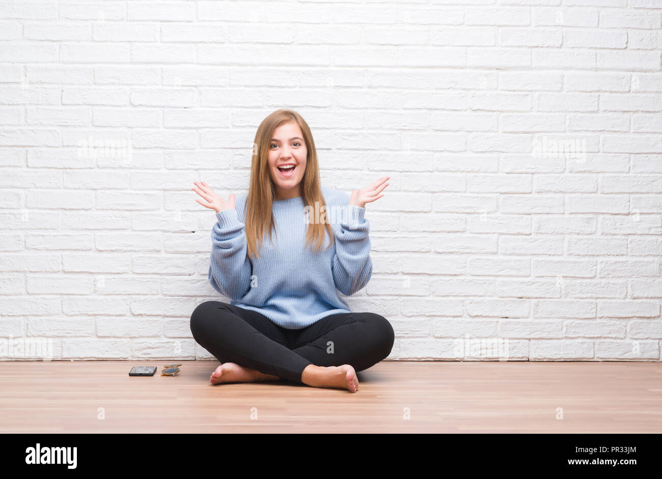 Young adult woman sitting on the floor in autumn over white brick wall ...