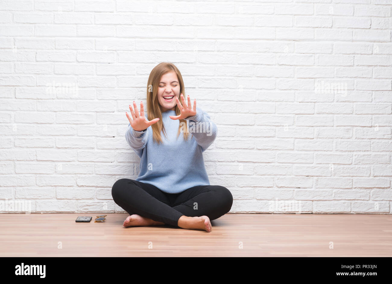 Young adult woman sitting on the floor in autumn over white brick wall ...