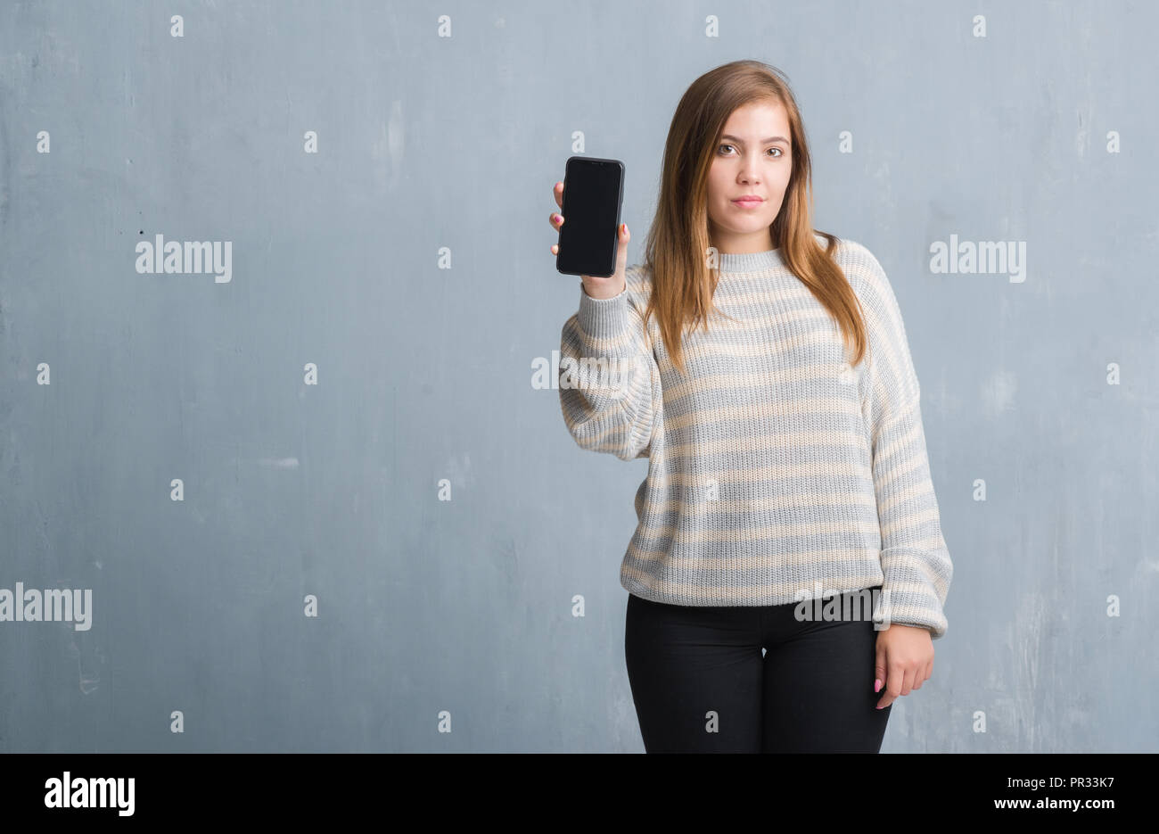 Young adult woman over grey grunge wall showing blank screen of ...
