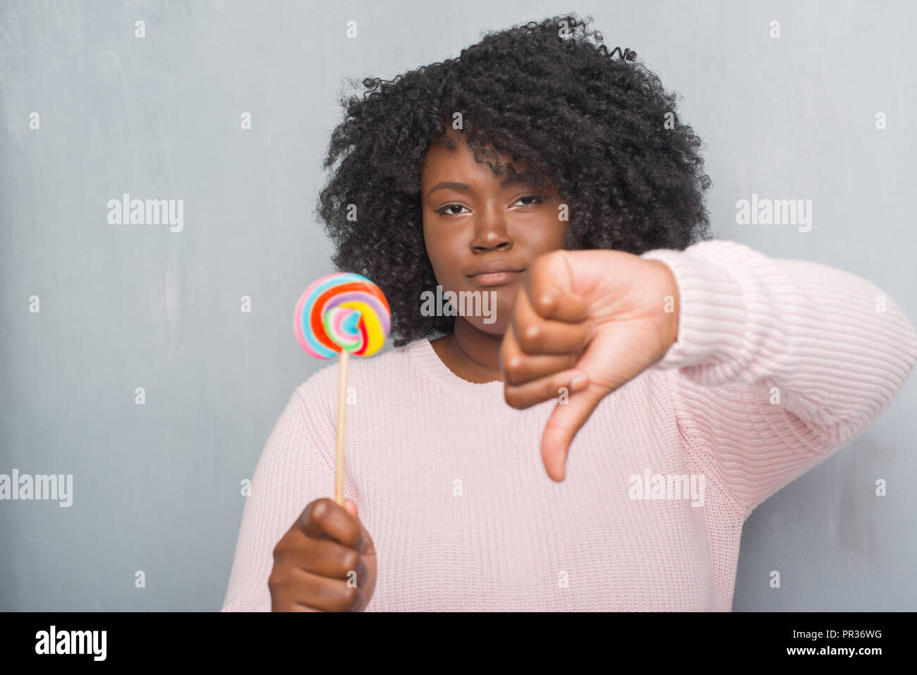 Young african american woman over grey grunge wall eating lollipop ...