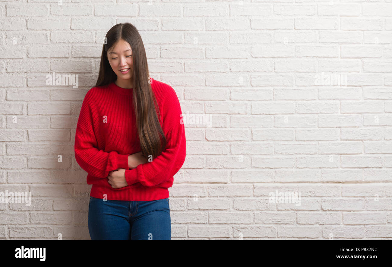 Young Chinese woman over brick wall with hand on stomach because nausea ...