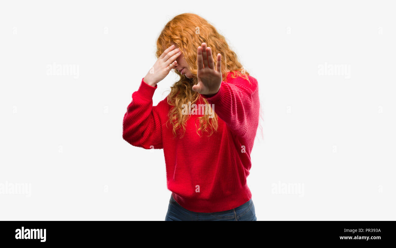 Young redhead woman wearing red sweater covering eyes with hands and ...