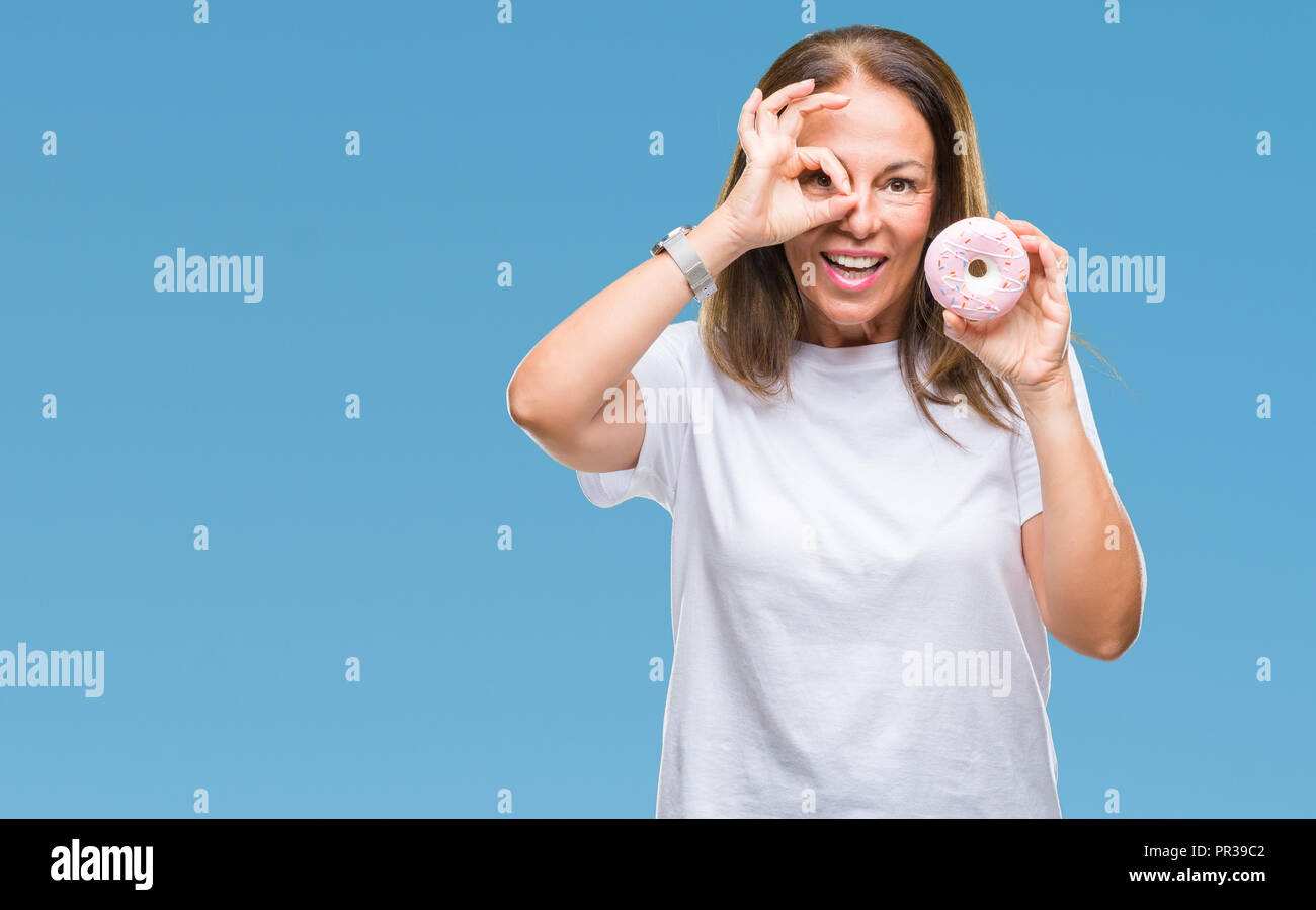 Middle age hispanic woman eating pink donut over isolated background ...
