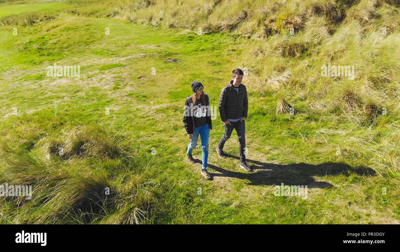 Aerial view over a young couple walking through the grass fields and ...