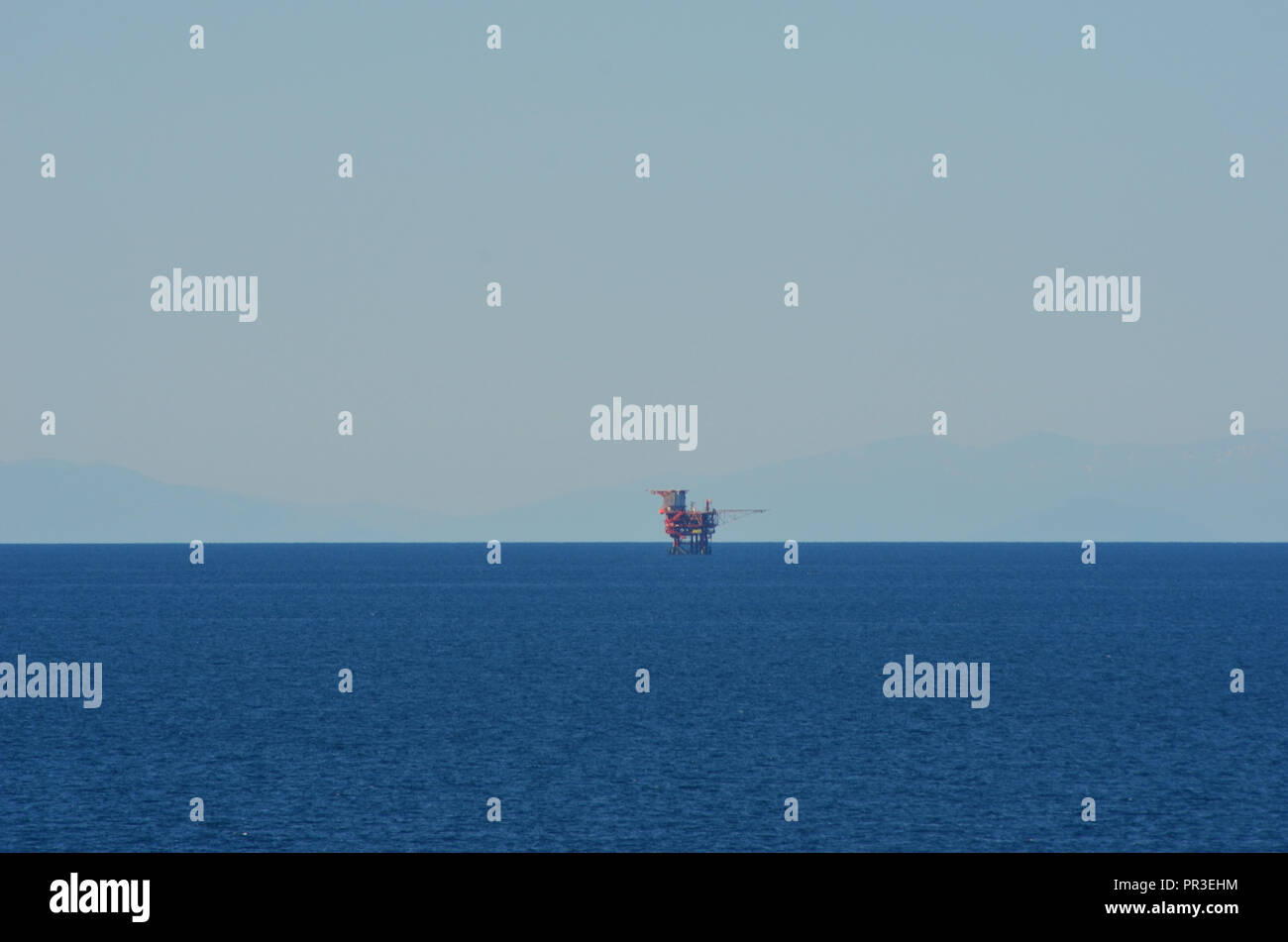 A small oil rig, mainly red in colour, is dwarfed by the expanse of the ...