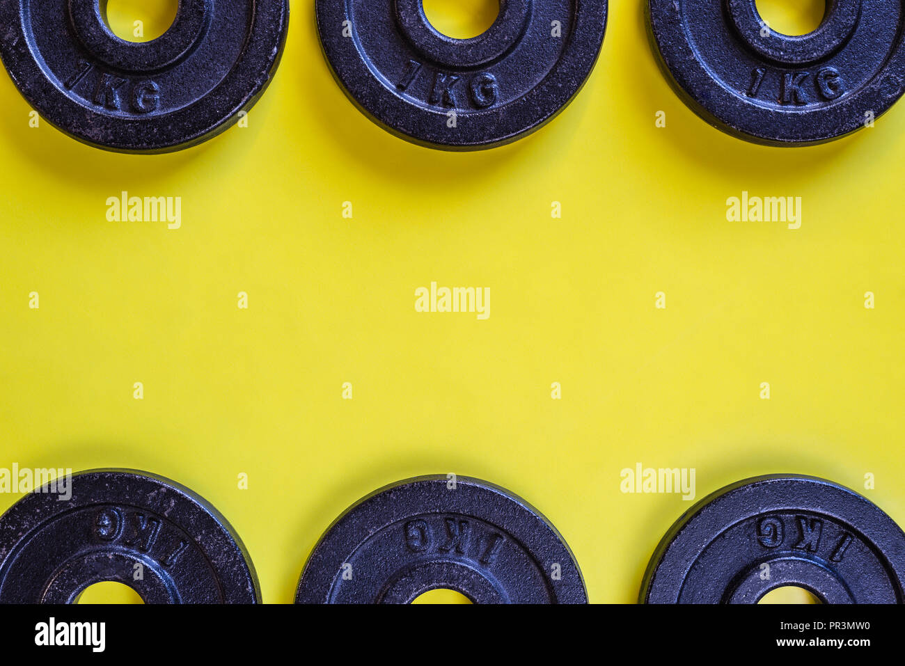 Black metal weights 1kg lying on a yellow background, flat view from ...