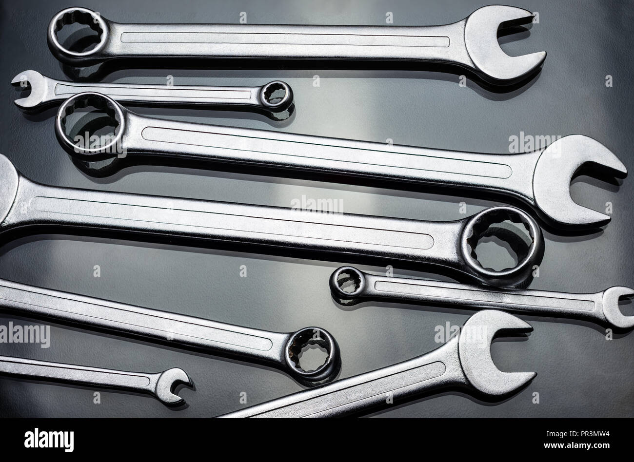 Metal flat wrenches lying on a black, shiny table, flat view from above ...