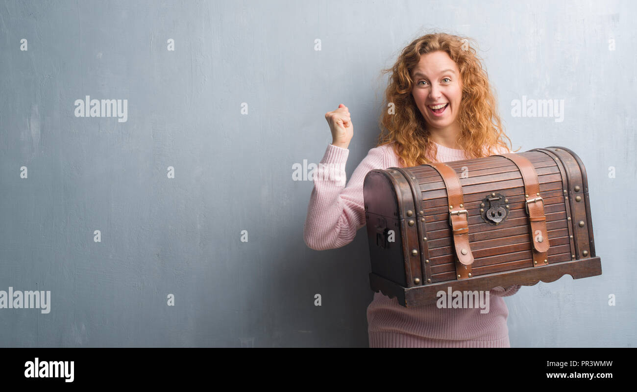 Young redhead woman holding vintage chest screaming proud and ...