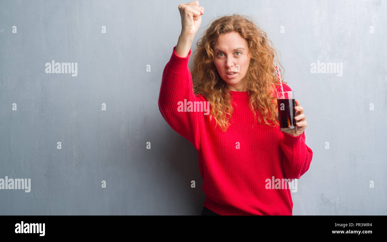Young redhead woman over grey grunge wall drinking soda refreshment ...