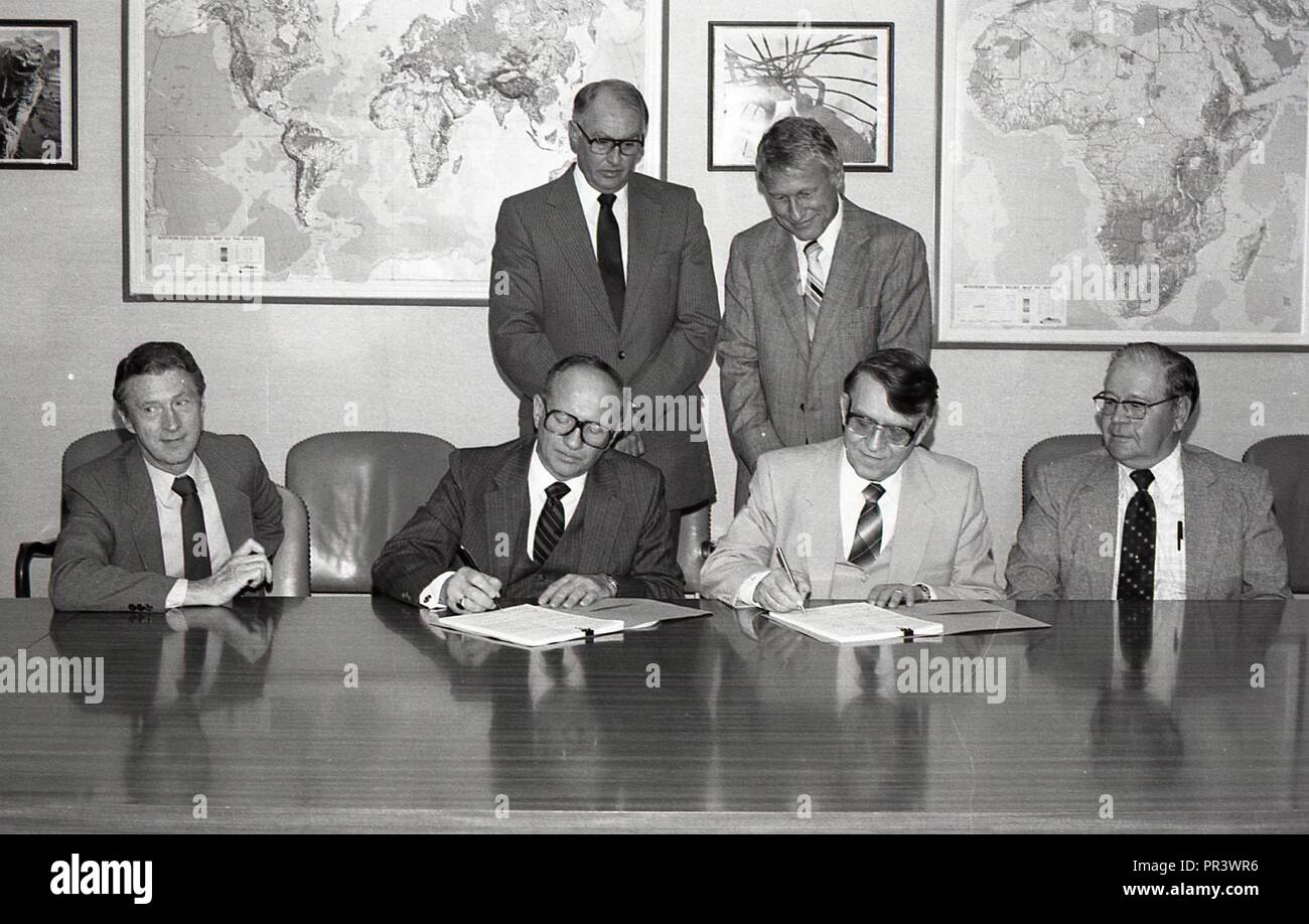 A GROUP OF MEN AT THE TABLE WITH TWO OF THE MEN SIGNING SOME PAPERS ...