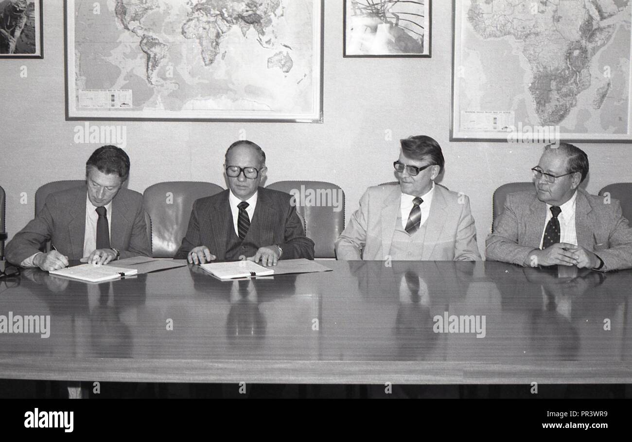 A GROUP OF MEN AT THE TABLE WITH ONE OF THE MEN SIGNING SOME PAPERS ...