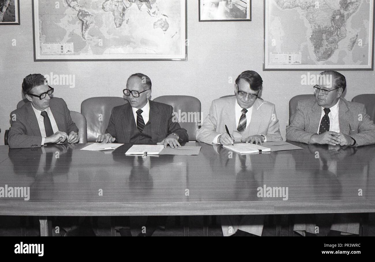 A GROUP OF MEN AT THE TABLE WITH ONE OF THE MEN SIGNING SOME PAPERS ...