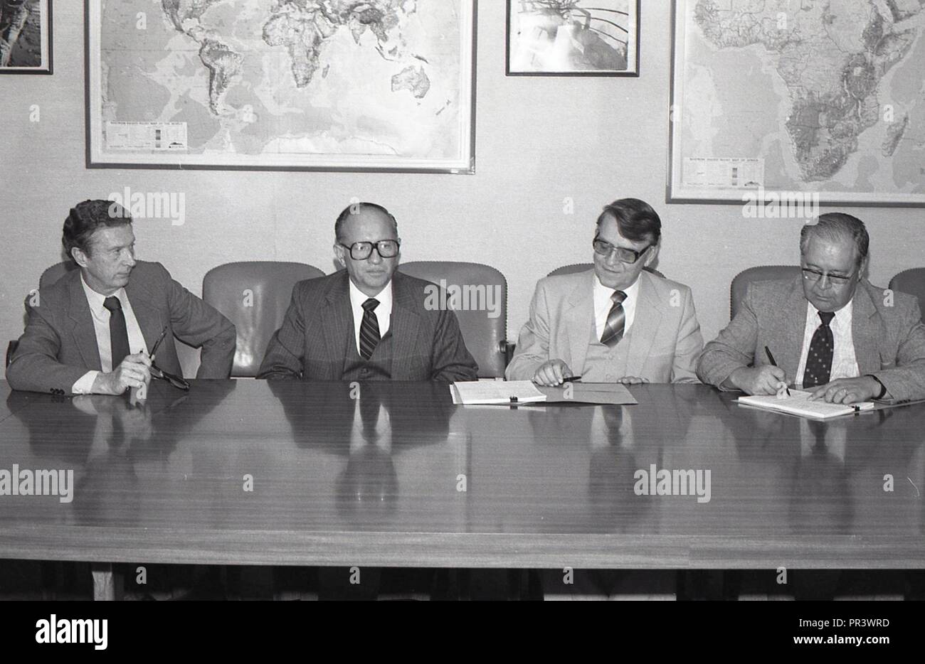 A GROUP OF MEN AT THE TABLE WITH ONE OF THE MEN SIGNING SOME PAPERS ...