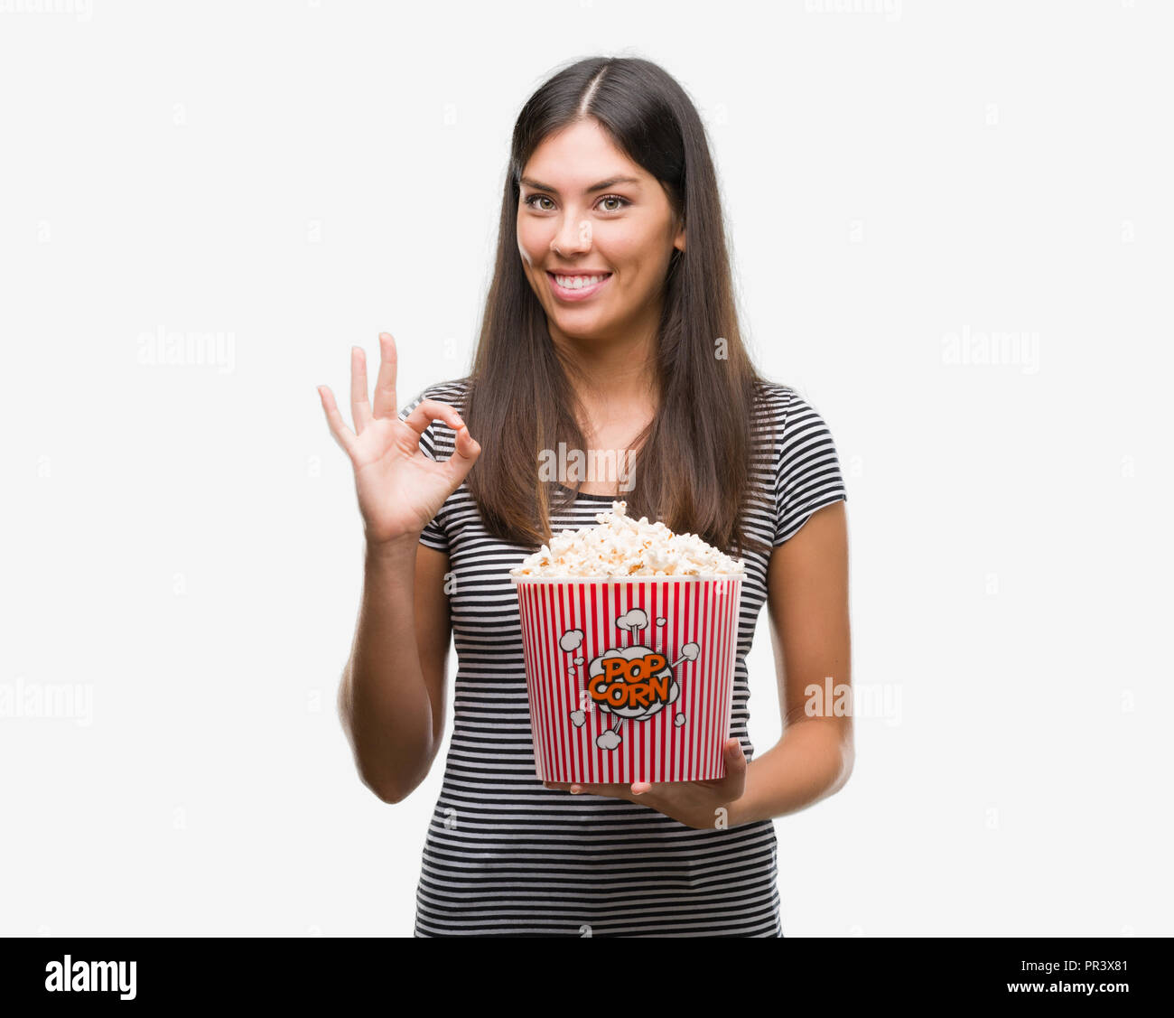 Young beautiful hispanic eating popcorn doing ok sign with fingers ...