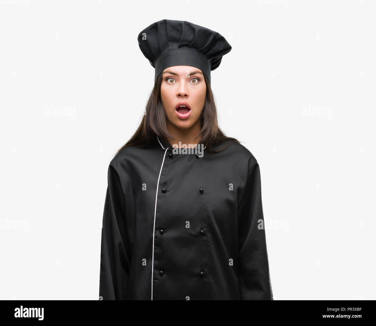 Young hispanic cook woman wearing chef uniform scared in shock with a ...