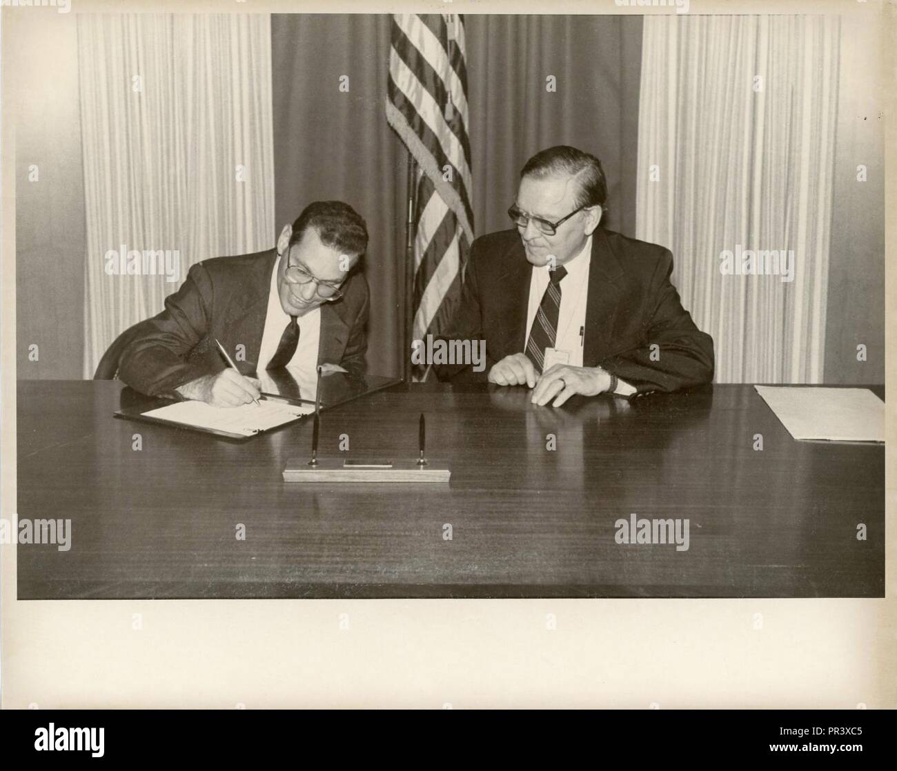 TWO MEN AT THE TABLE WITH ONE OF THE MEN SIGNING SOME PAPERS Stock ...