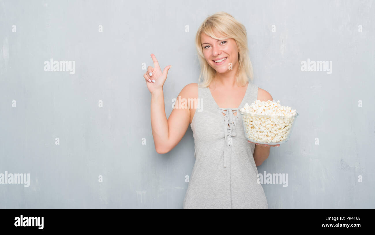Adult caucasian woman over grunge grey wall eating pop corn very happy ...