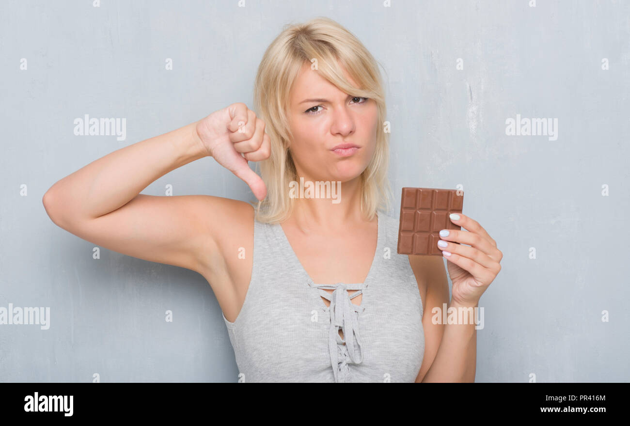 Caucasian adult woman over grey grunge wall eating chocolate bar with ...