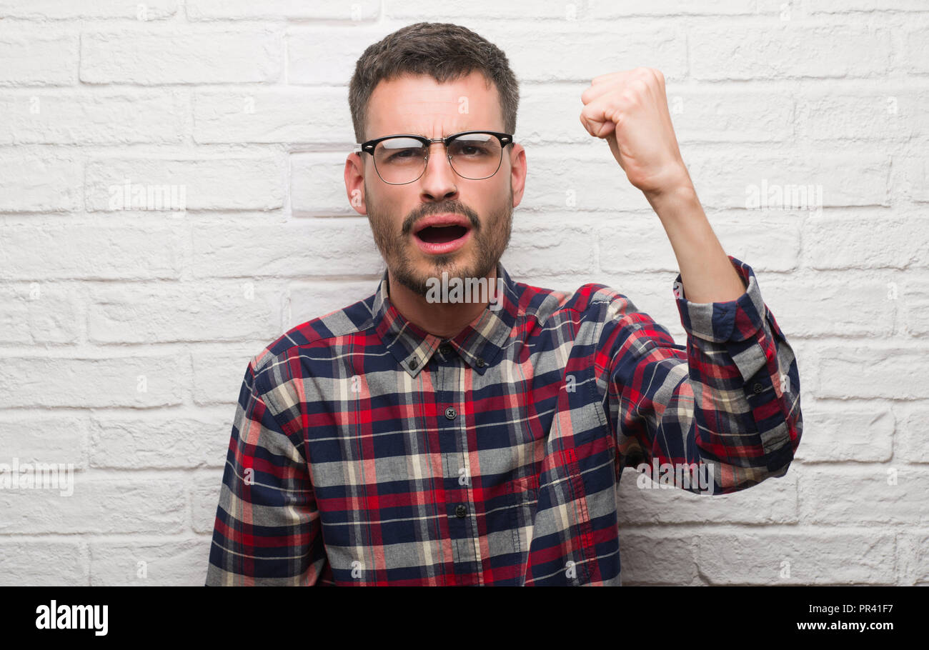 Young adult man standing over white brick wall annoyed and frustrated ...