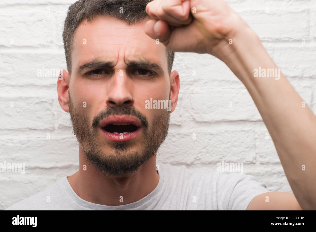 Young adult man standing over white brick wall annoyed and frustrated ...