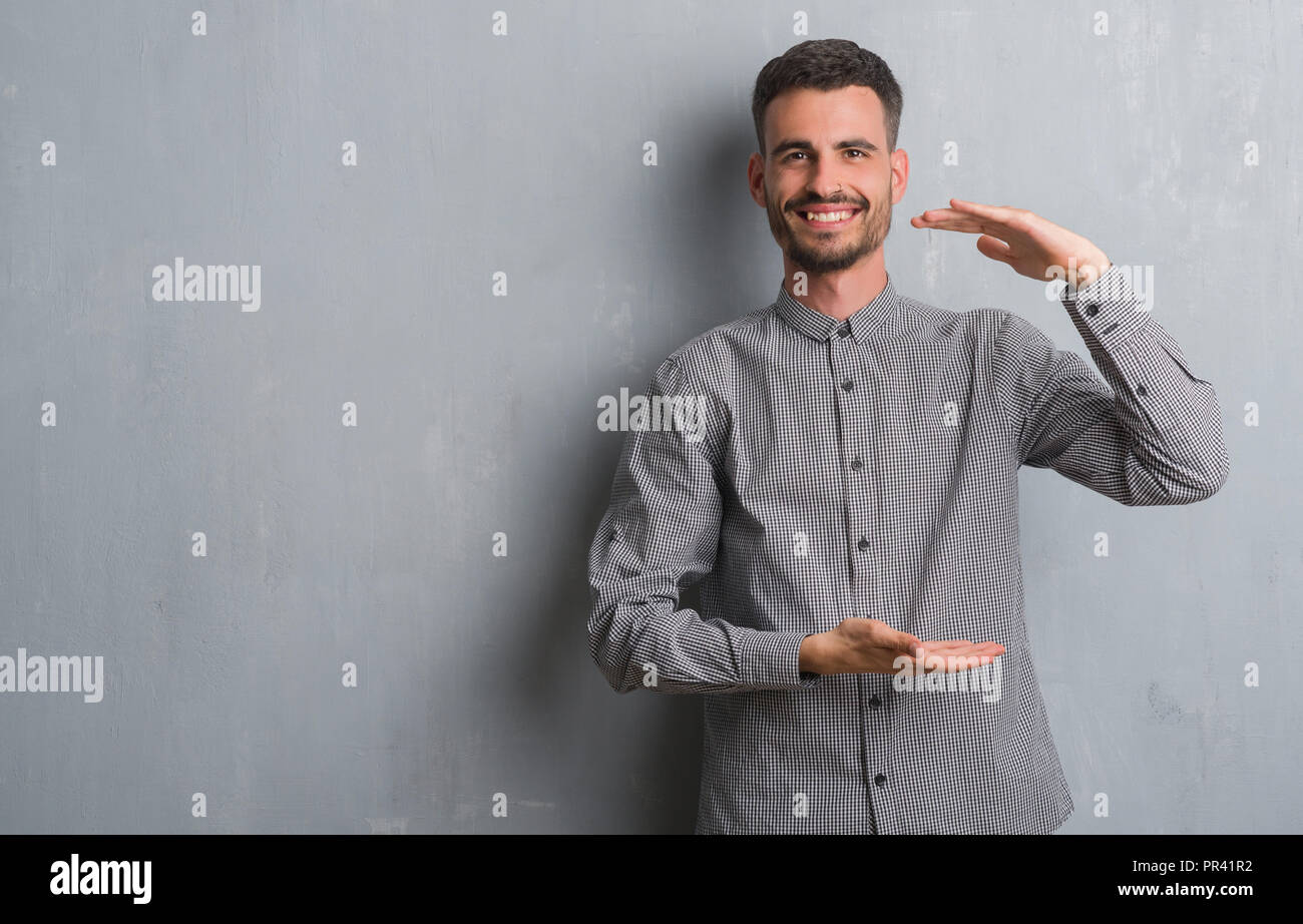 Young adult man standing over grey grunge wall gesturing with hands ...