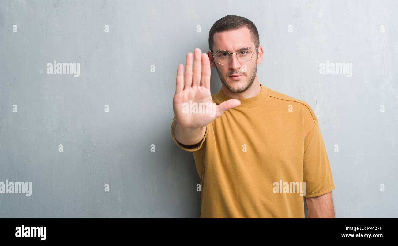 Young caucasian man over grey grunge wall with open hand doing stop ...