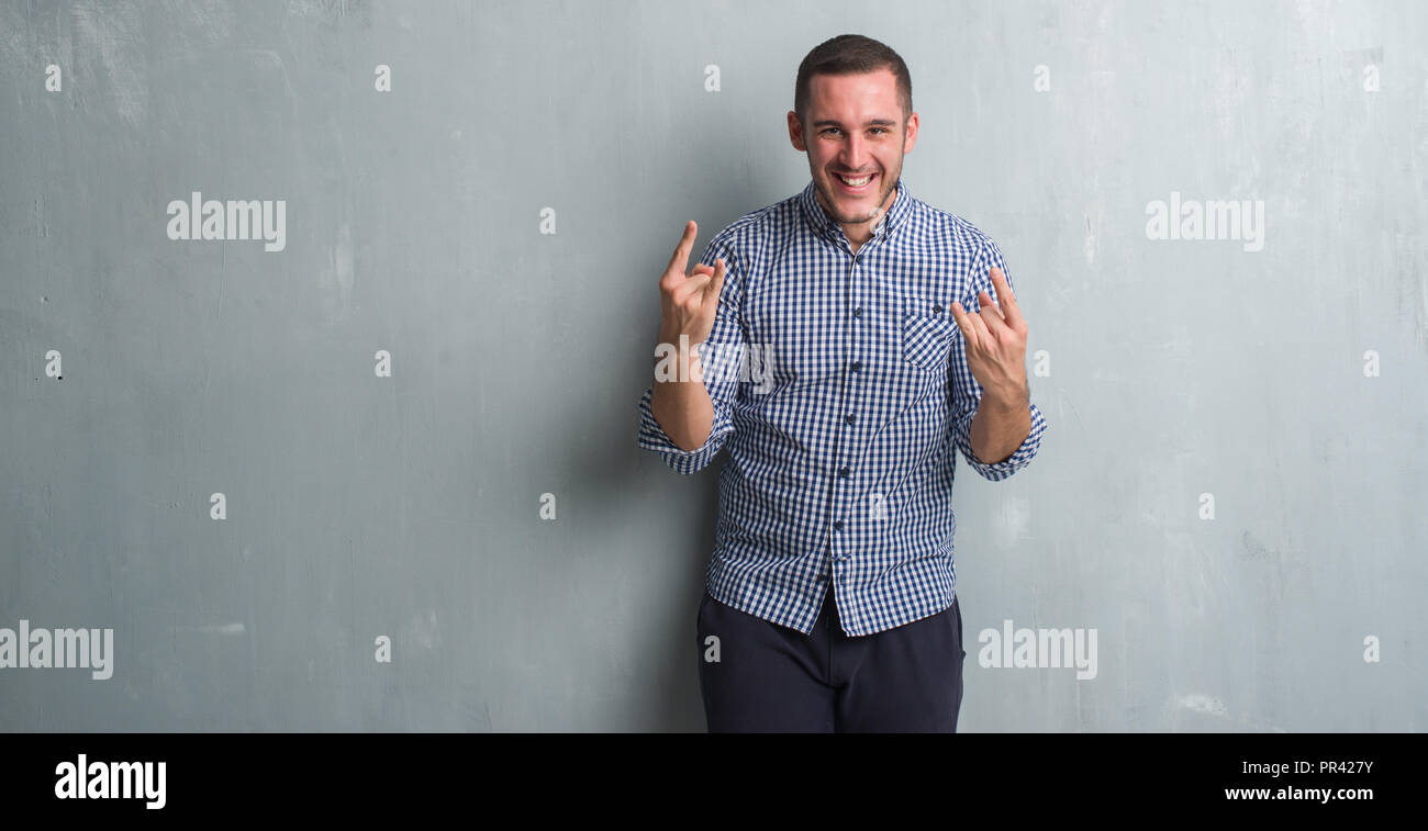 Young caucasian man over grey grunge wall shouting with crazy ...