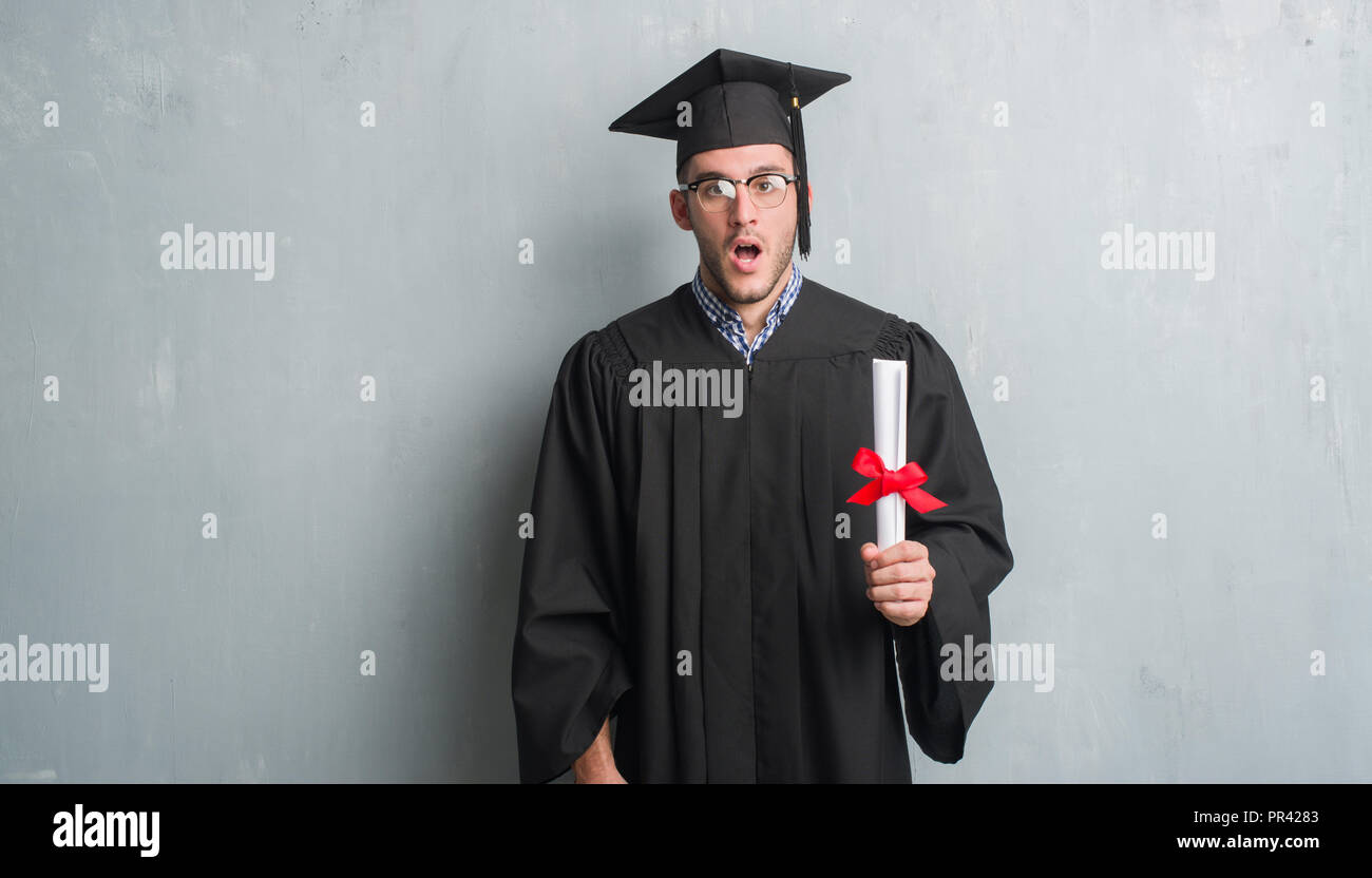 Young caucasian man over grey grunge wall wearing graduate uniform ...
