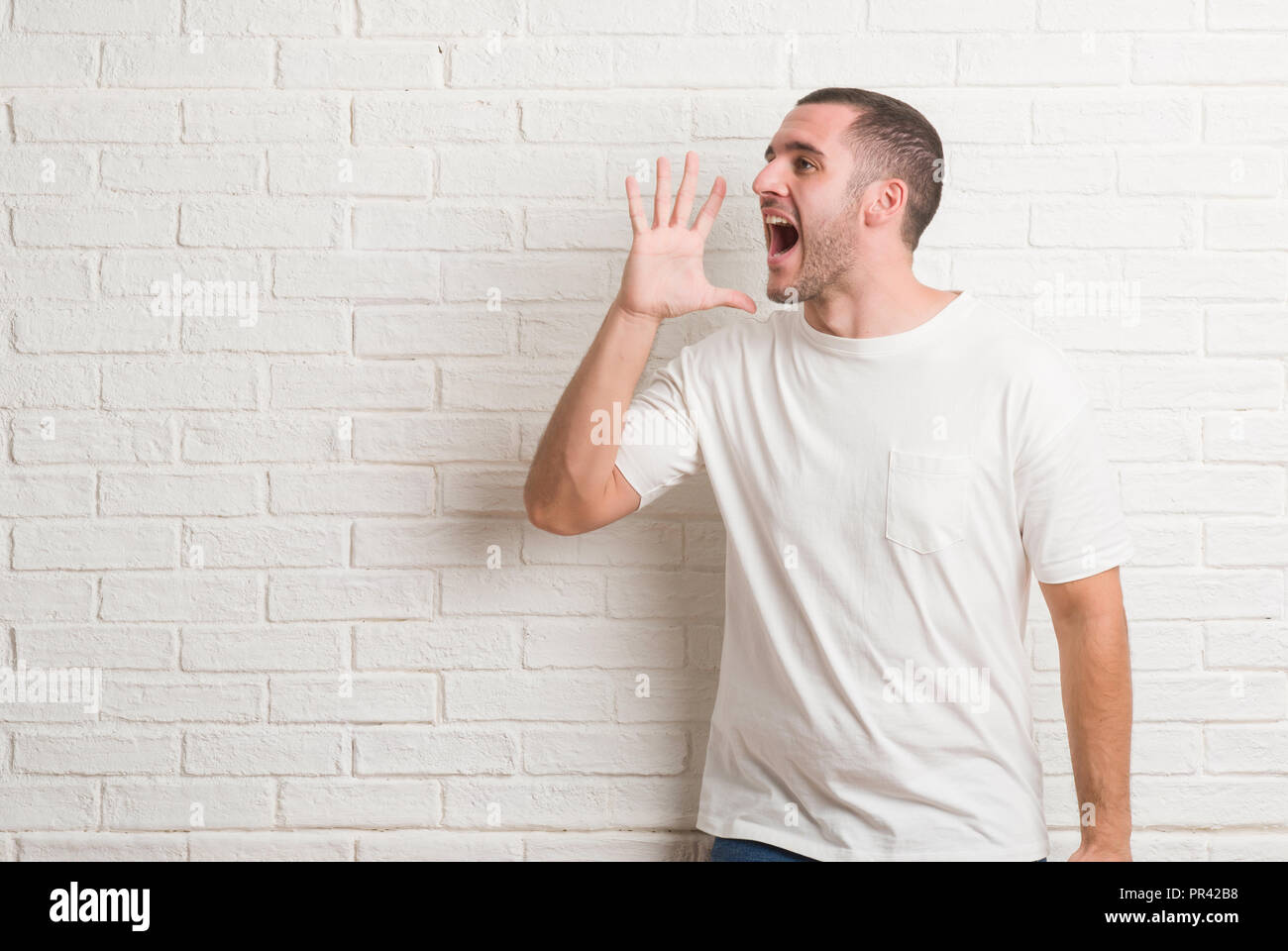 Young caucasian man standing over white brick wall shouting and ...