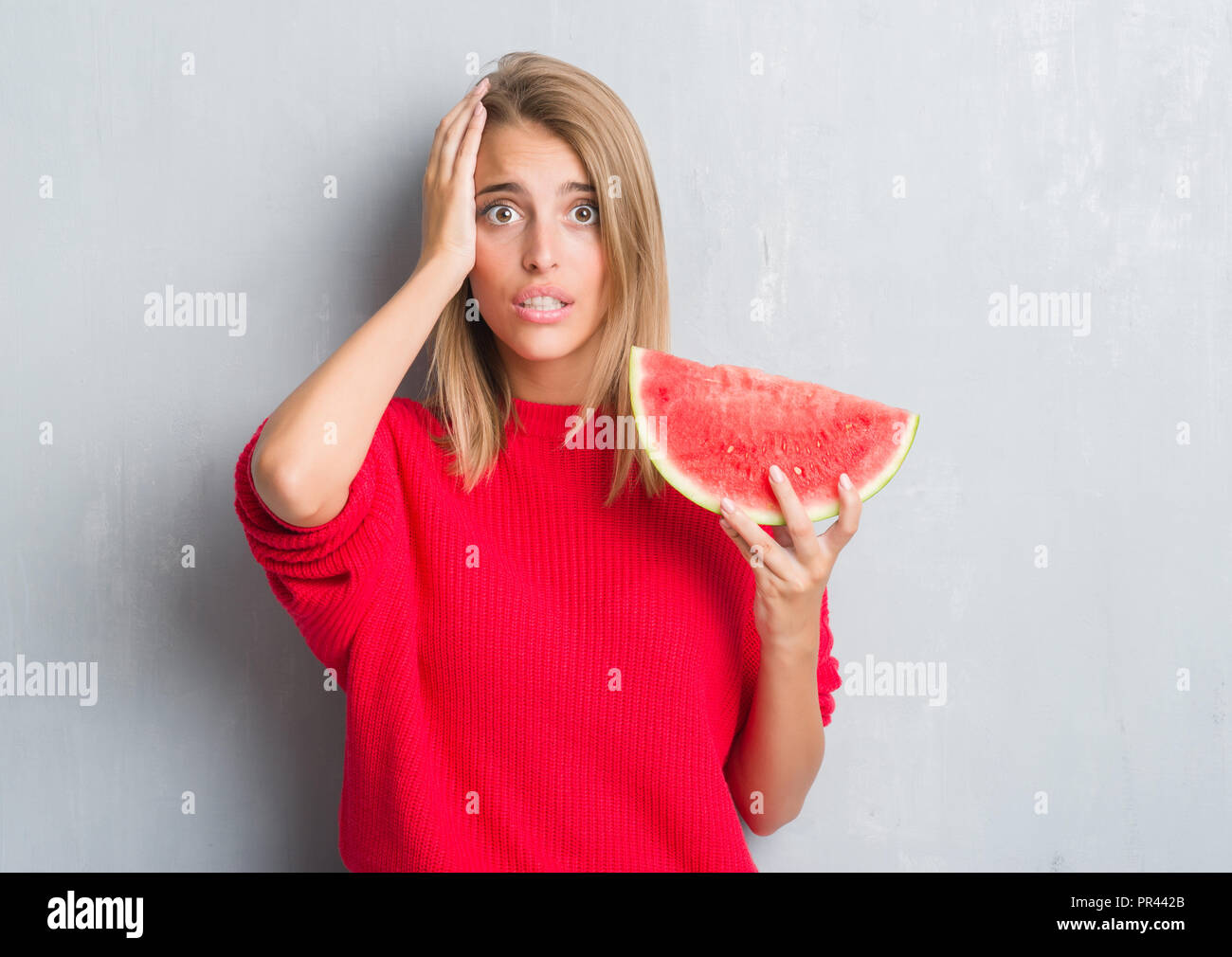 Beautiful young woman over grunge grey wall eating water melon stressed ...