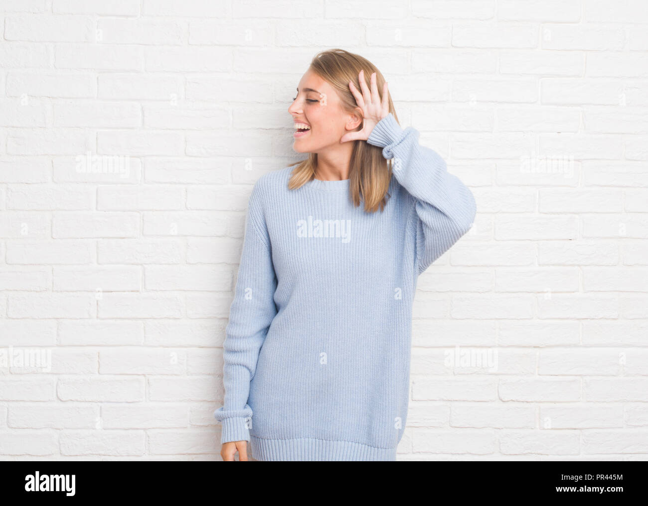 Beautiful young woman over white brick wall smiling with hand over ear ...
