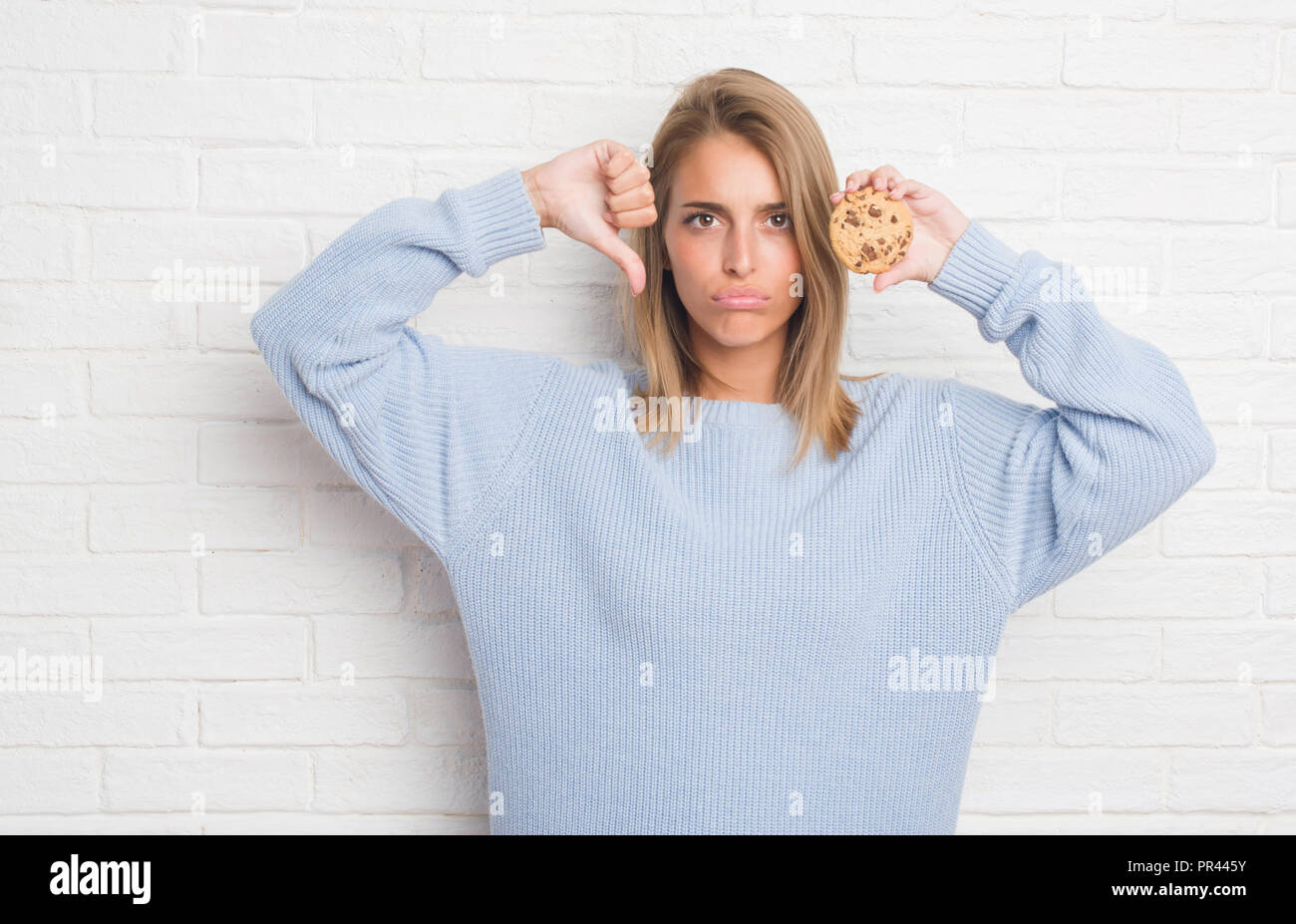 Beautiful young woman over white brick wall eating chocolate chip cooky ...