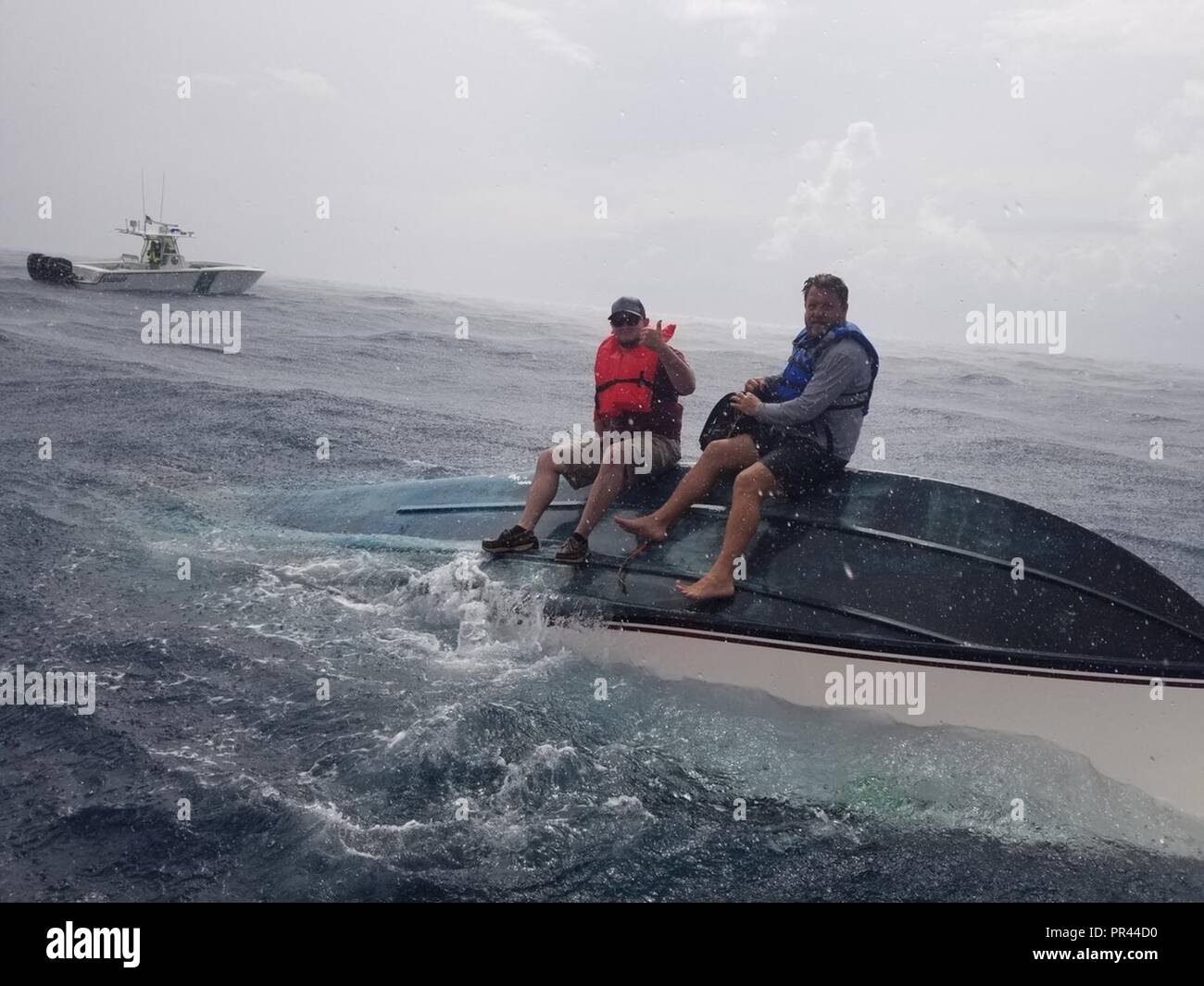 Two boaters sit on the hull of their capsized 23-foot boat in the water ...