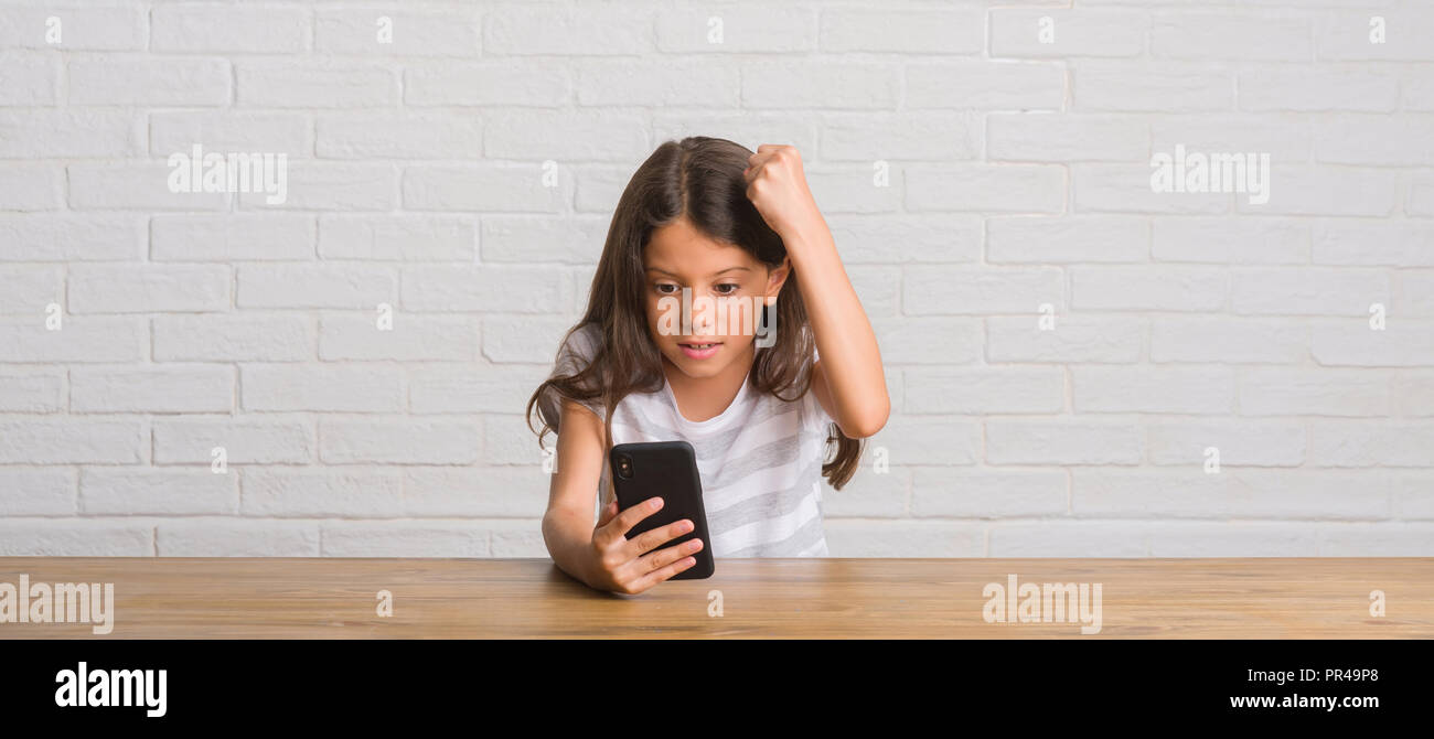 Young hispanic kid sitting on the table using smartphone annoyed and ...