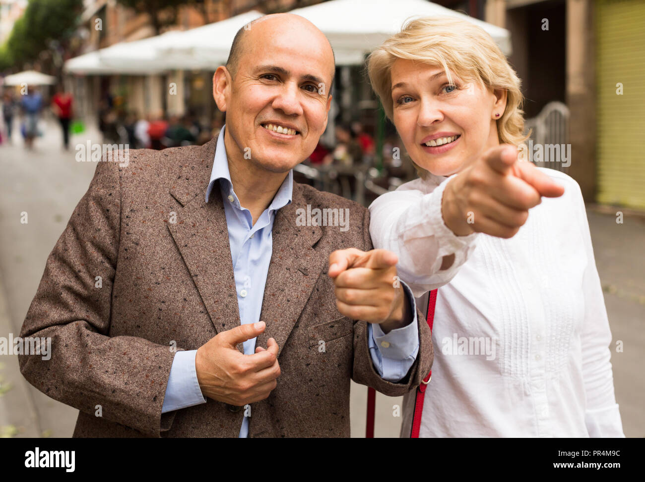 glad senior couple taking promenade and point their fingers outdoors ...