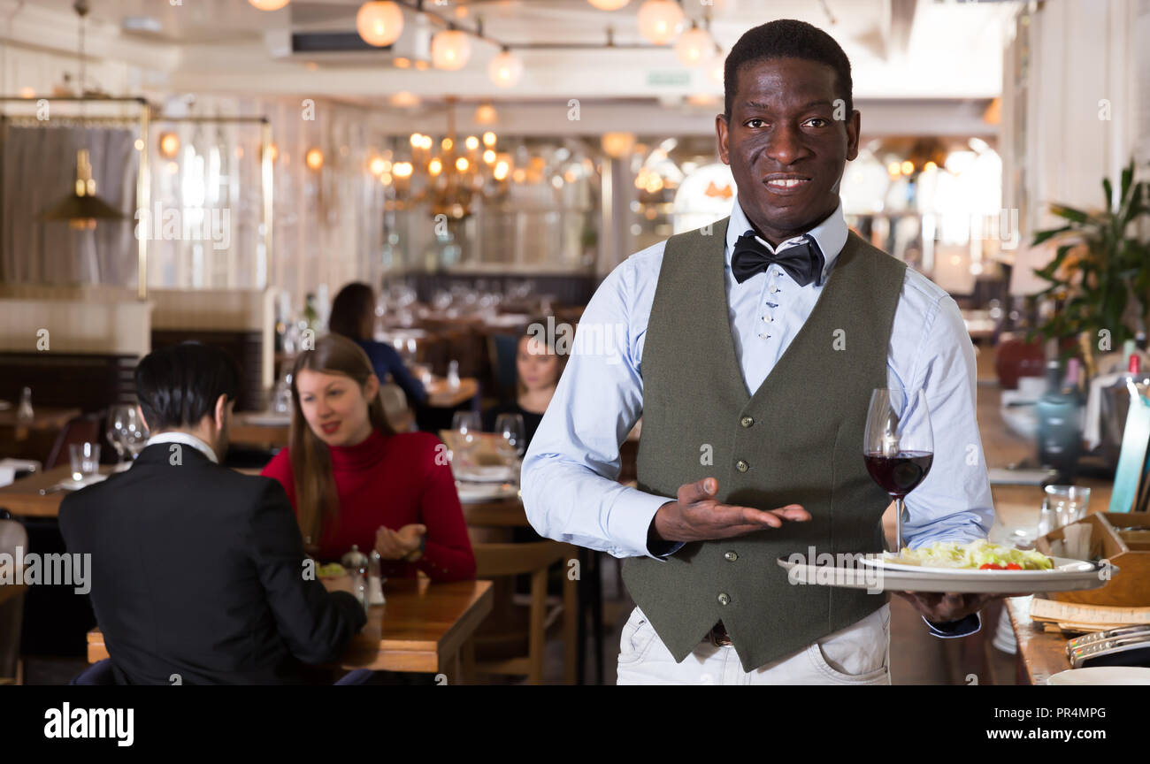 Adult waiter who is standing with order in hall of luxurious restaurant ...