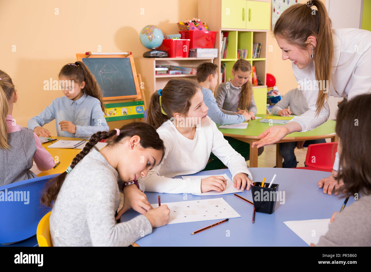 Woman teacher helping to group of pupils drawing at classroom Stock ...