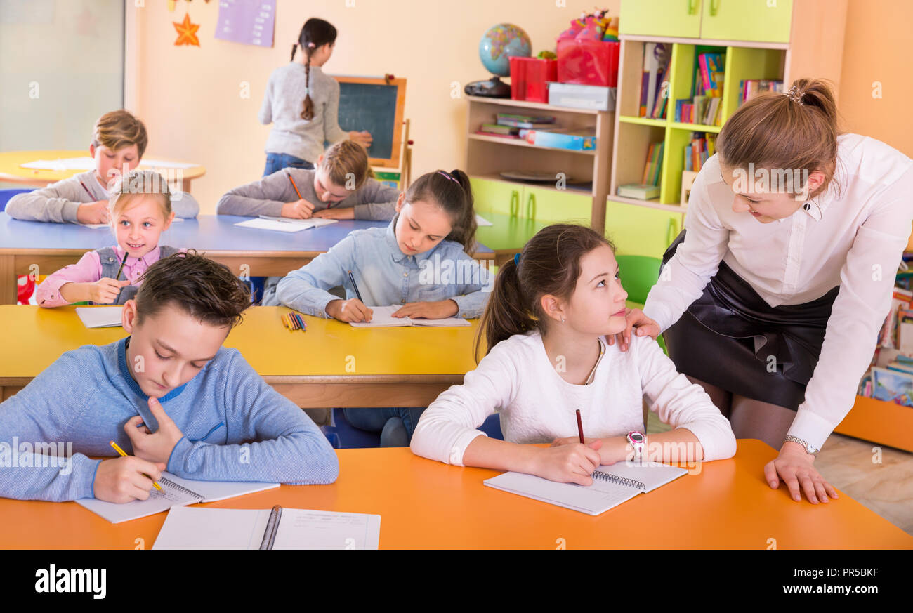 Friendly teacher woman helping children during lesson at schoolroom ...