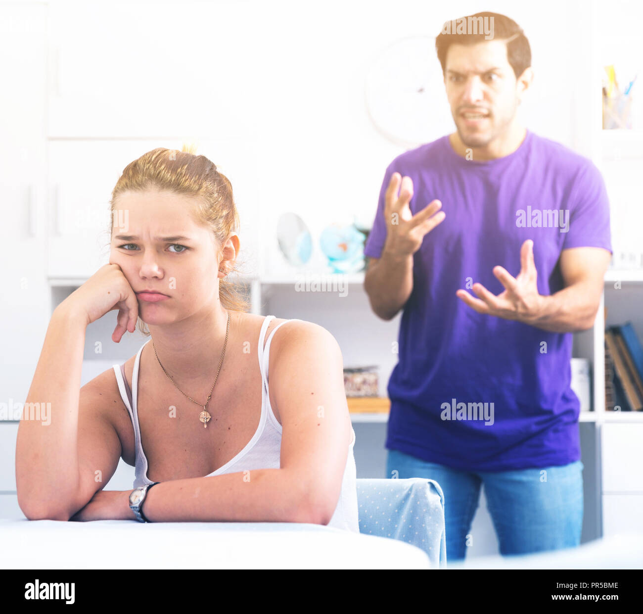 Upset young woman sitting at home table with disgruntled man behind ...