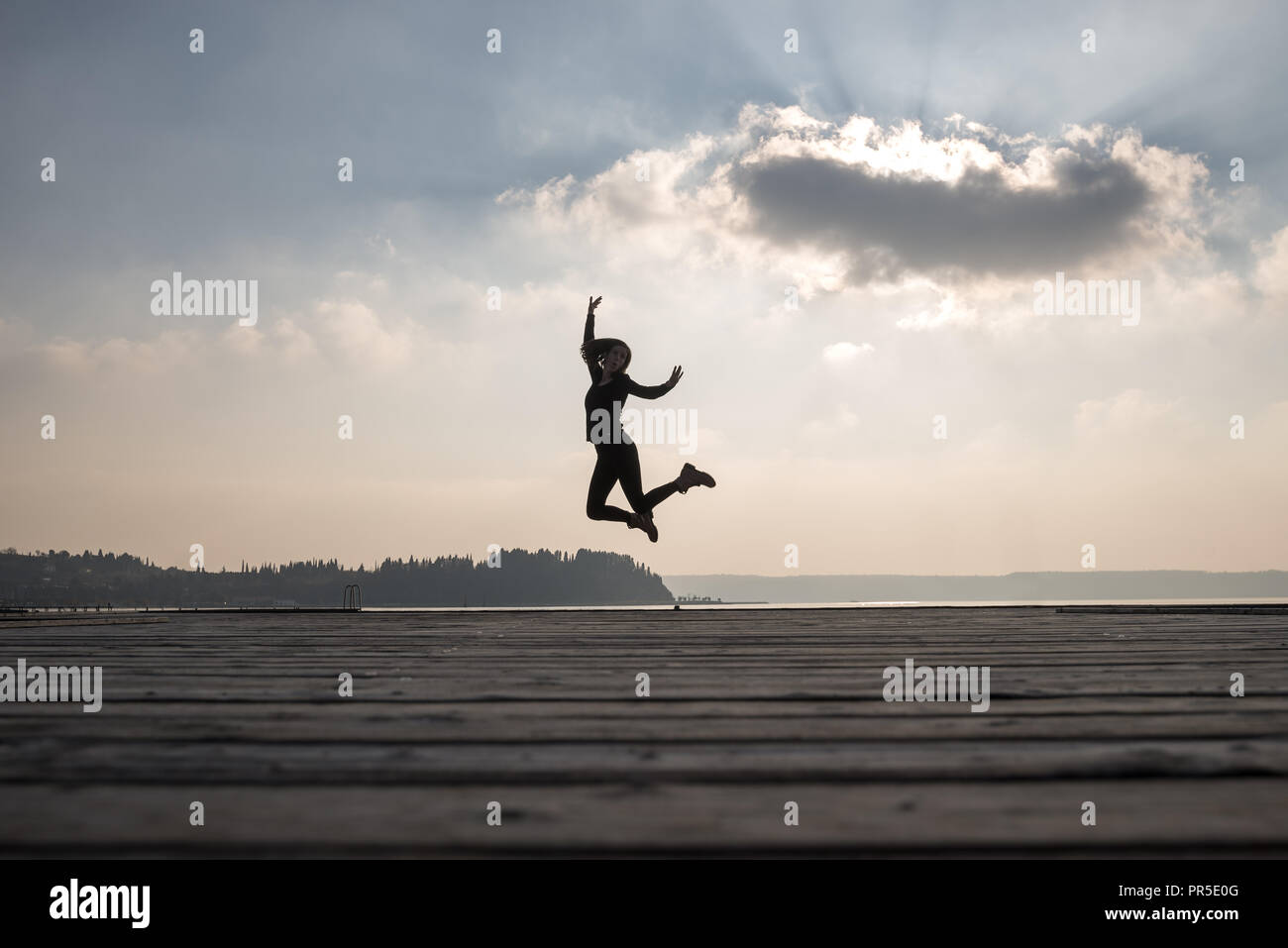 Happy woman jumping in air against sky with sun behind cloud Stock ...