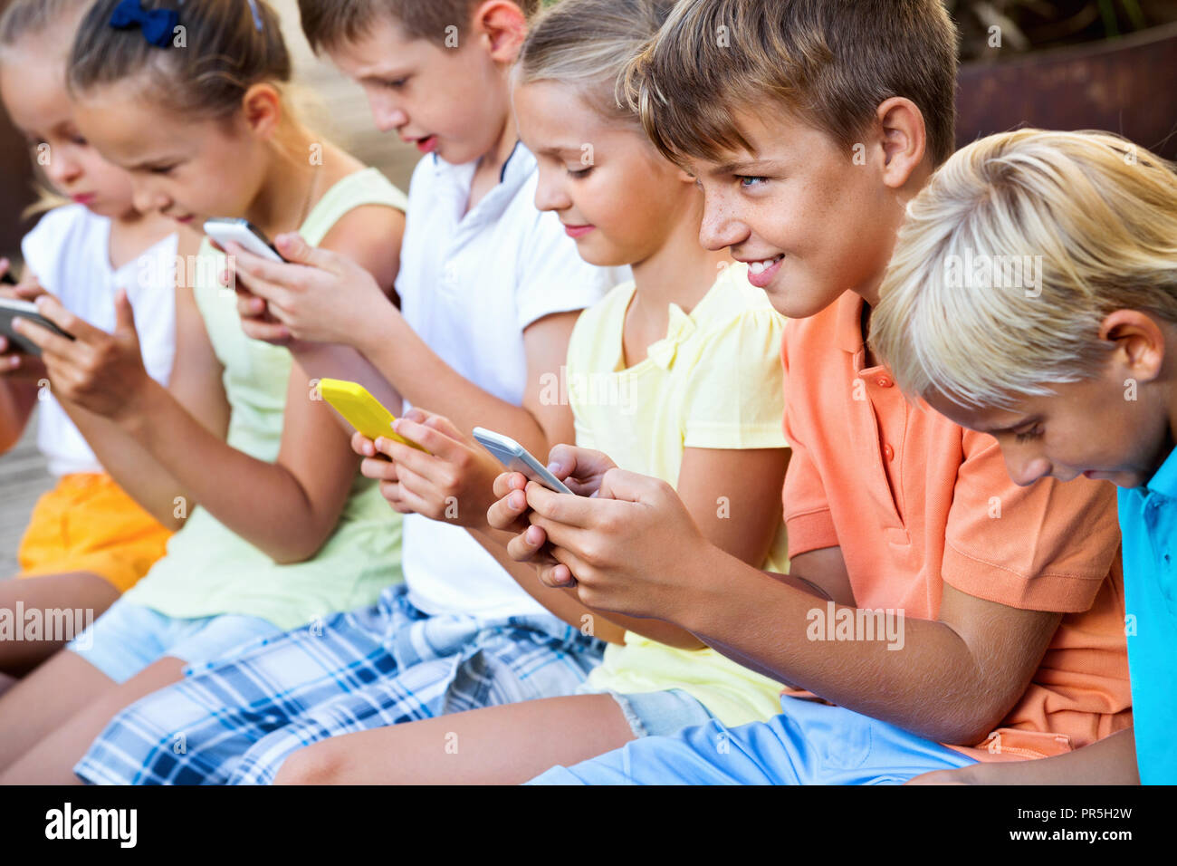 Busy serious children holding smartphones in hands and sitting together ...