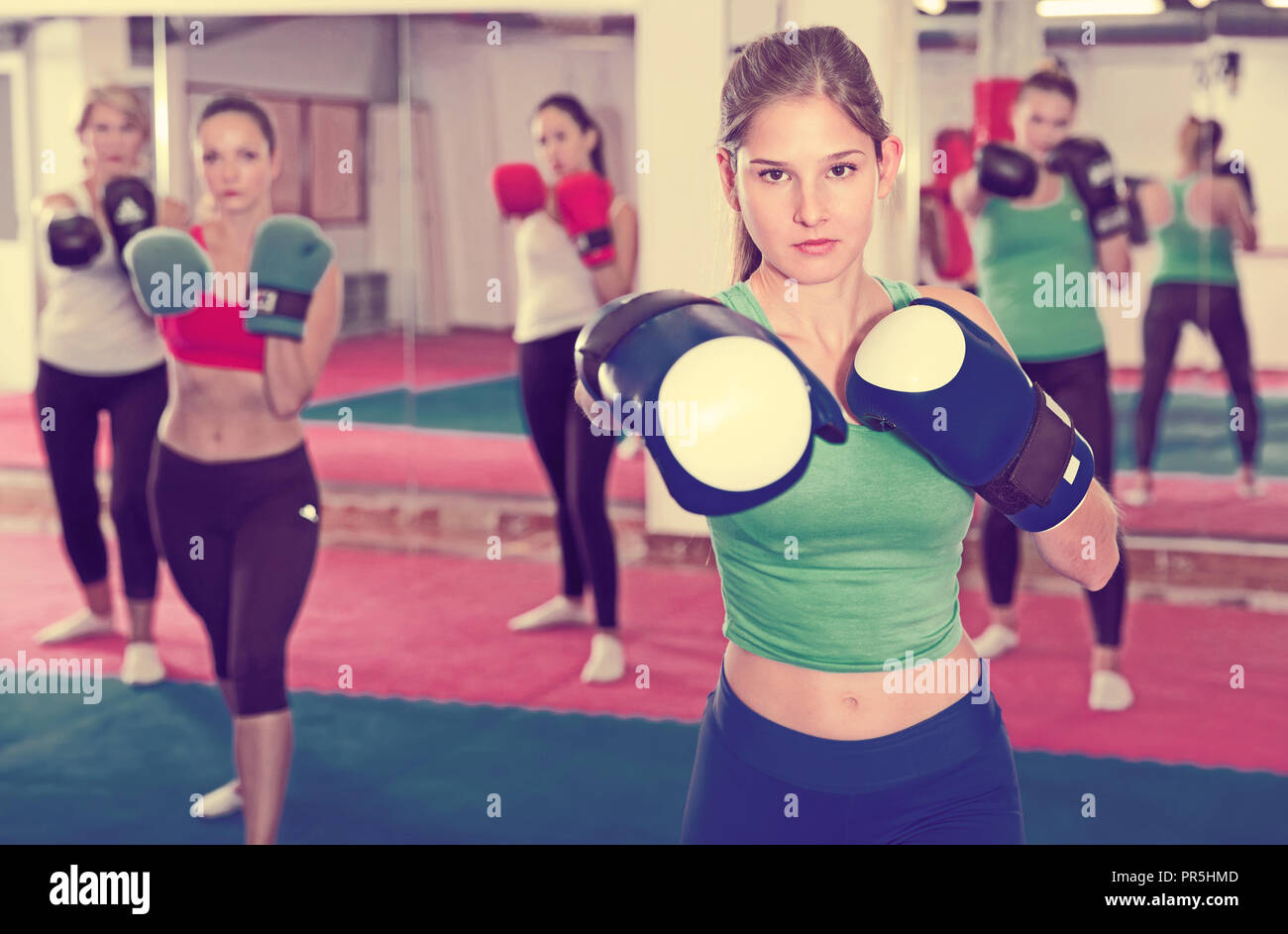Portrait of female who is boxing exercises with group in sporty gym ...