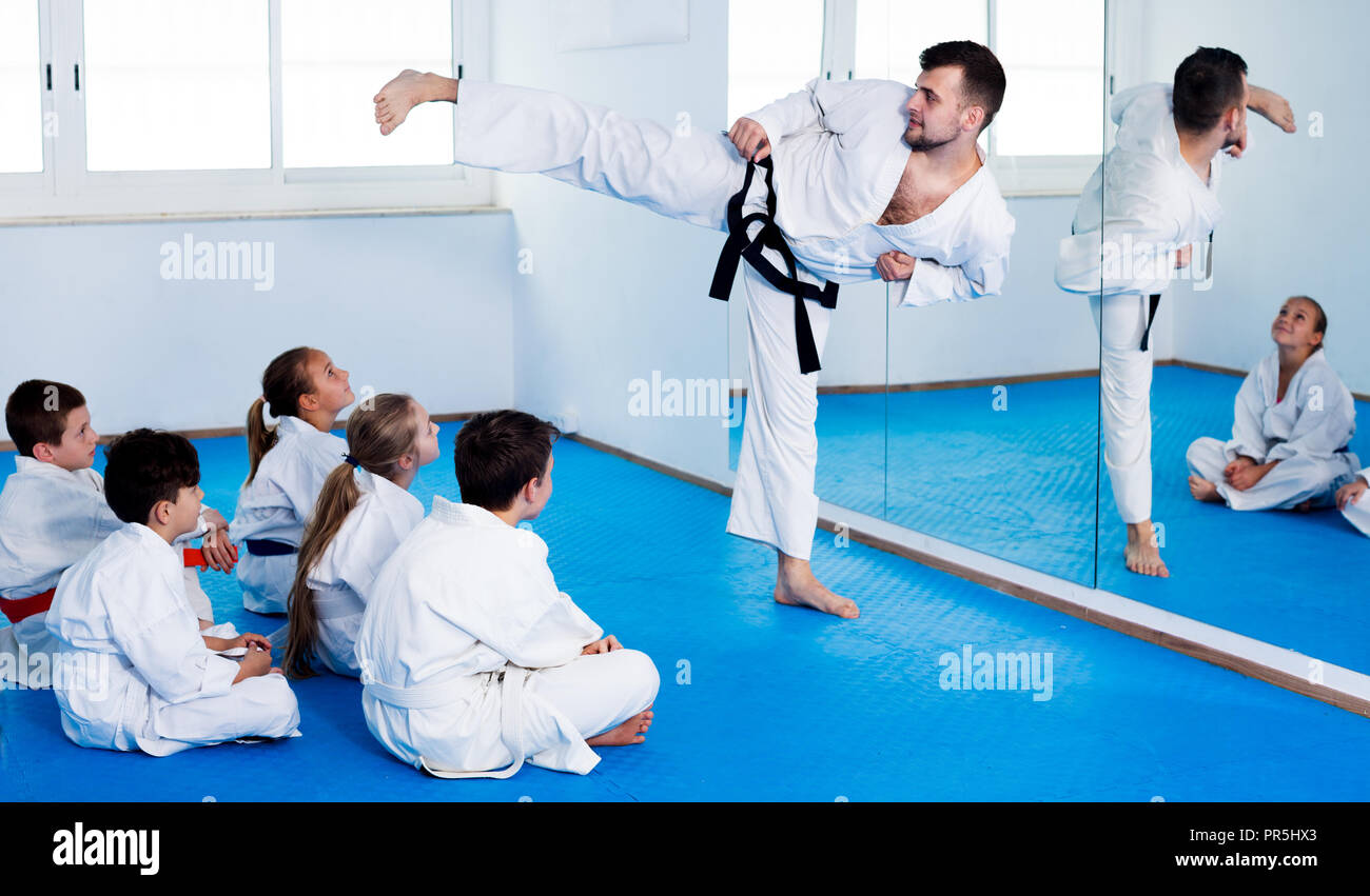 Glad male coach explaining new maneuvers to children in karate class ...