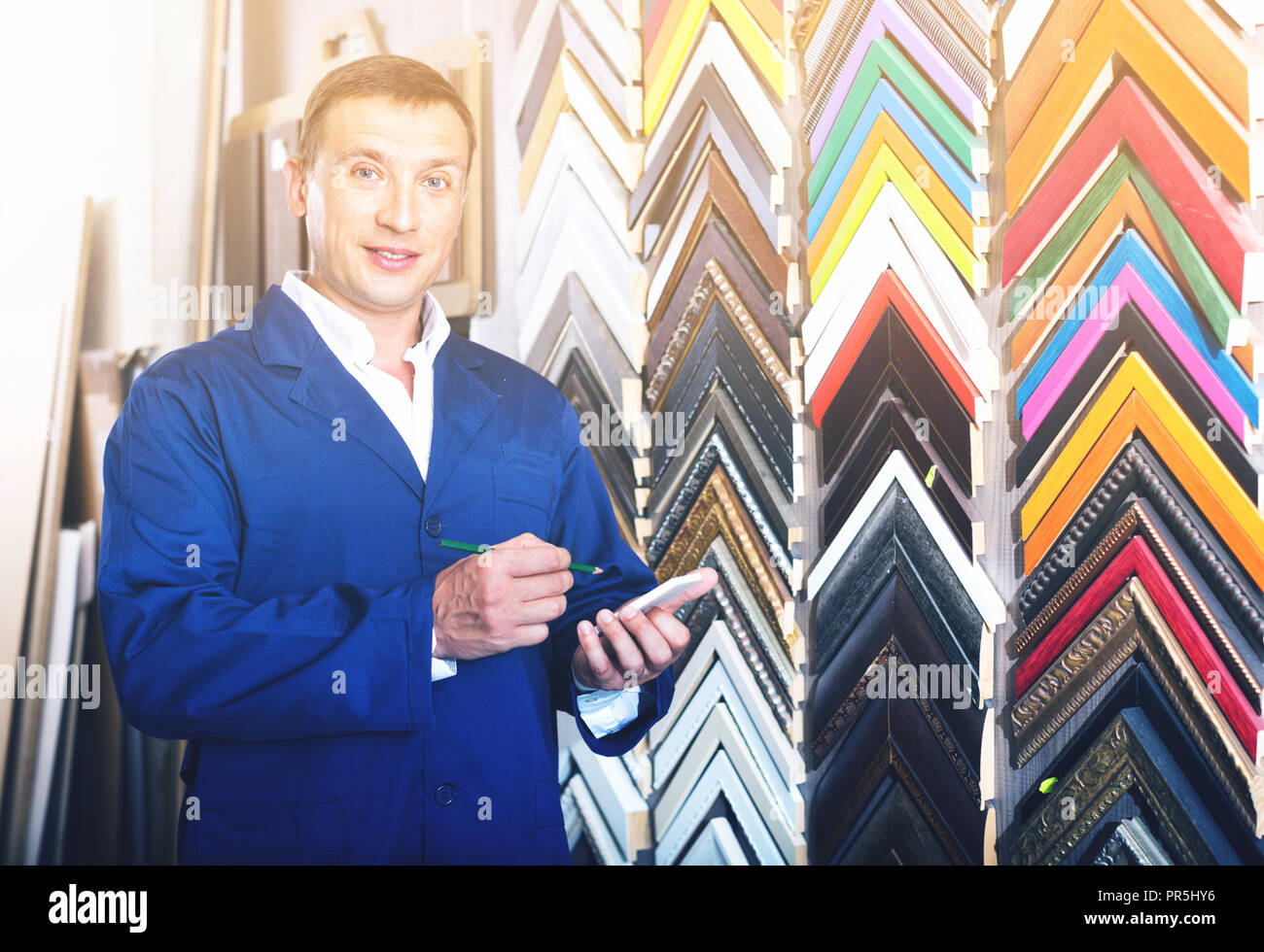 Smiling positive glad man worker holding picture frame details on ...
