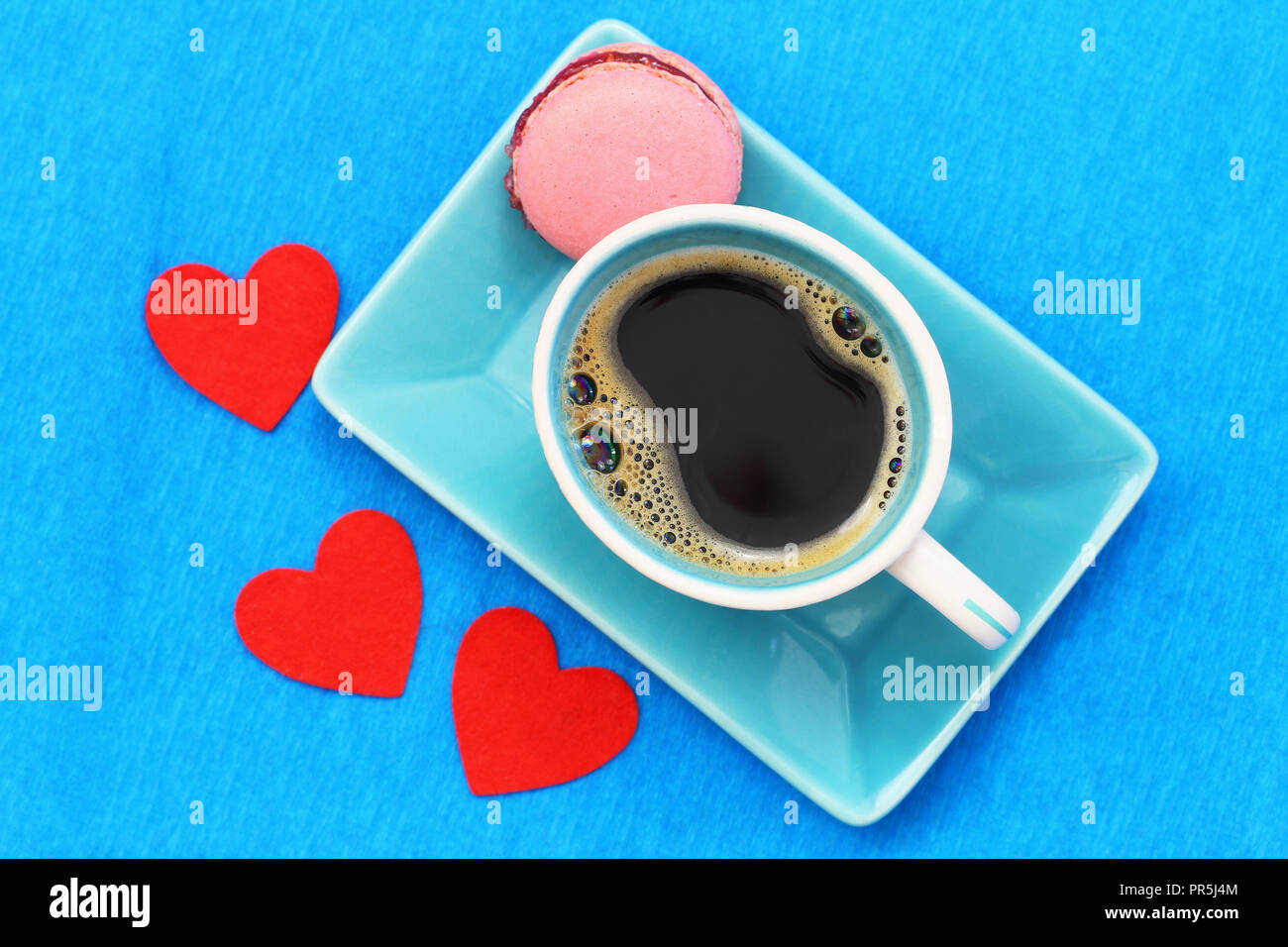 Black coffee in cup, raspberry macaroon and three red hearts on blue ...