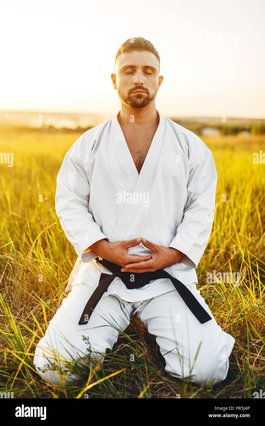 Male karate fighter sitting on the ground in summer field. Martial art ...