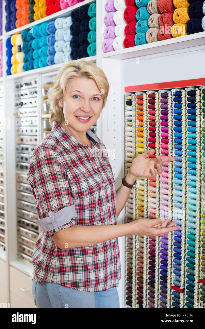 European mature woman choosing various colorful stitching spools in ...